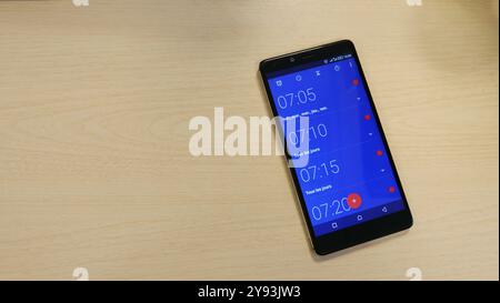 A smartphone displaying multiple alarm times on a wooden surface ...
