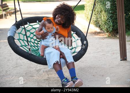 Happy mother smiles at baby sitting on bed in room. Motherhood. Mothers ...