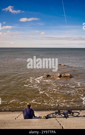 Cyclist resting on steps of seawall at high tide,UK Stock Photo - Alamy