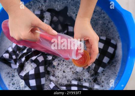 Woman pouring detergent into cap over basin with clothing, closeup ...