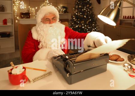 Santa Claus with typewriter and cup of cacao writing Christmas story at ...