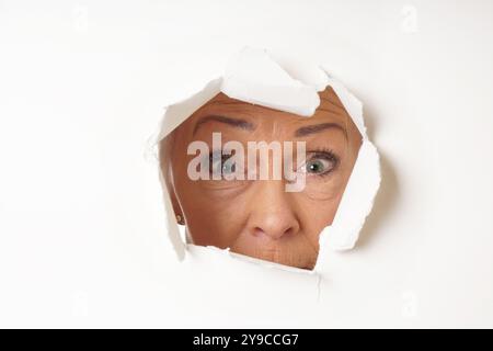 Staring senior woman peering through transparent screen at office ...
