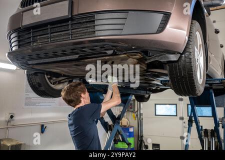 car mechanic standing under lifted car and fixing car in garage Stock ...