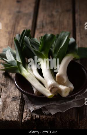 A bunch of green leeks in a brown bowl on a wooden table. Photo in a ...