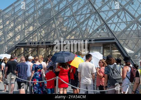 people in scorching midday sun stand in line to enter the louvre museum ...