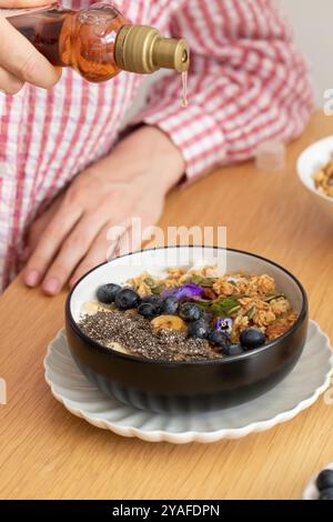 A woman pours maple syrup on granola and Greek yogurt. Healthy ...