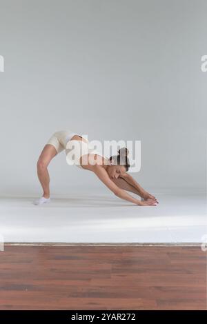 Female in an elegant beige workout ensemble, lifting her leg high in a ...
