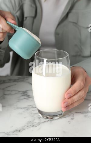 Making protein cocktail. Woman adding powder into glass with milk at ...