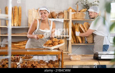 Young woman employee puts croissants in window, arranges display of ...