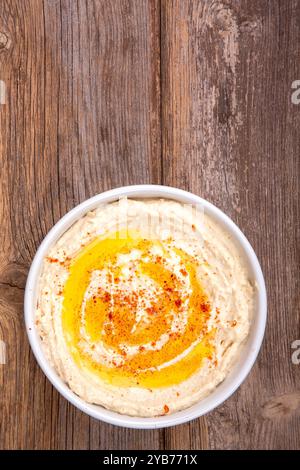 Creamy hummus on rustic wooden plate. Fresh ingredients surround ...