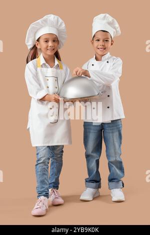 Cute little Asian chefs with cloche on beige background Stock Photo - Alamy
