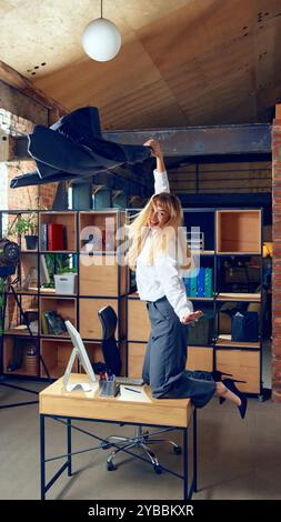 Emotional woman dancing her desk, throwing her jacket into air, smiling ...