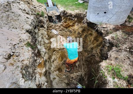 Homeowner throws soil into wheelbarrow while digging hole for septic ...