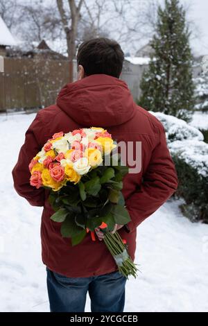 The boy hides flowers behind his back and smiles. A child with a ...