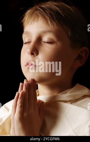 child praying to God with hands together with black background with ...