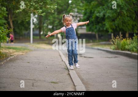 The girl walks along the sidewalk, keeping her balance, arms ...