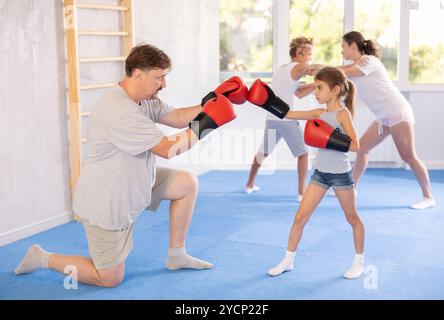Girl and dad are boxing in gym, father helps child to work out force of ...