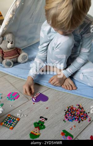 child makes figures from multi-colored thermo mosaics lying on floor in ...