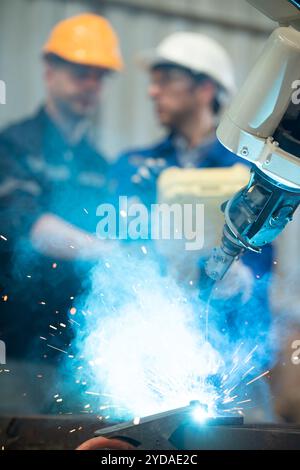 Both of engineers are manipulating a welding robot hand. By combining ...