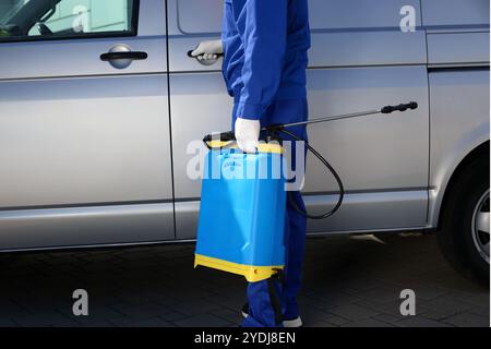 Pest control worker with spray tank near gray minibus outdoors, closeup ...