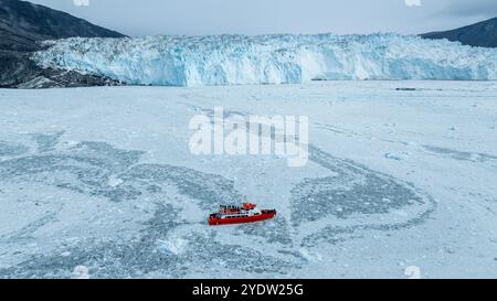 Aerial of a little ship floating between the ice below the Eqi glacier ...