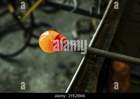 Glass-blower man working with hot orange glass to make a blown glass ...