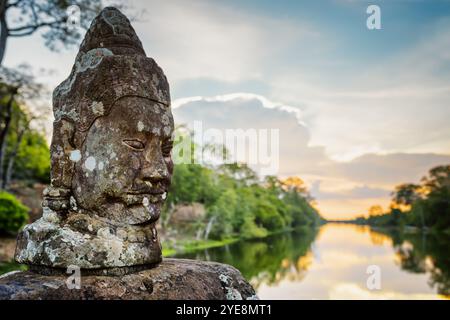 Mossy stone face Asura and sunset over moat. Angkor, Cambodia Stock ...