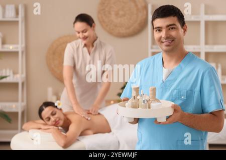 Male massage therapist with spa supplies pointing at something on beige ...