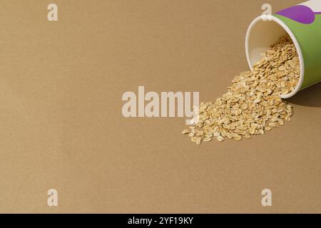 A container with spilled dry oatmeal onto a brown paper background with ...