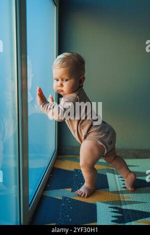 A baby boy tries to stand up by the window. The child learns to stand ...
