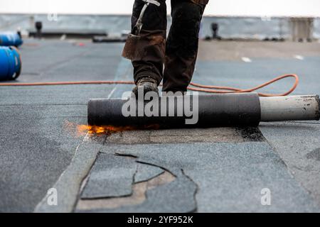 professional roofer at work securing rolled tar paper with a blowtorch ...