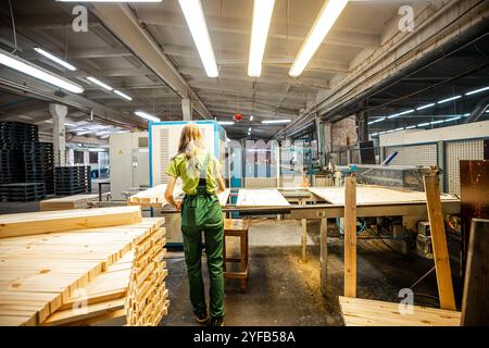 A worker in green overalls operates a machine in a woodworking factory ...