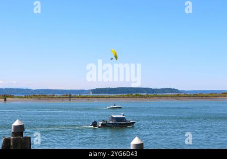 Boats underway with a yellow canopied paraglider over Jetty Island ...