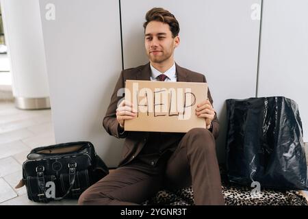 Homeless millennial businessman in suit sitting on city street holding ...