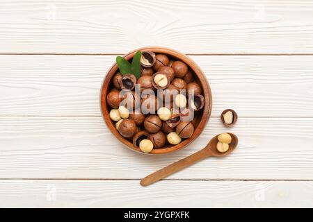 Wooden bowl and spoon with tasty macadamia nuts on blue background ...