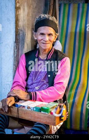An old Filipino market worker sells cigarettes on the street in a ...