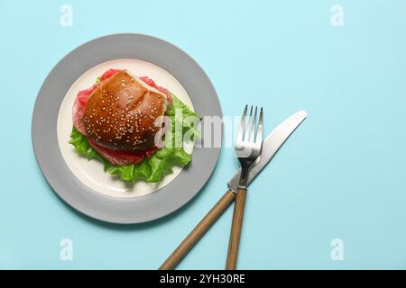 Plate with tasty burger and plastic on blue background. Microplastic ...