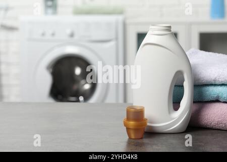 Laundry detergent, cap and stacked clean towels on grey table, space ...