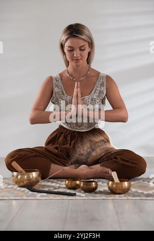 Beautiful meditating young woman with Tibetan singing bowl at home ...