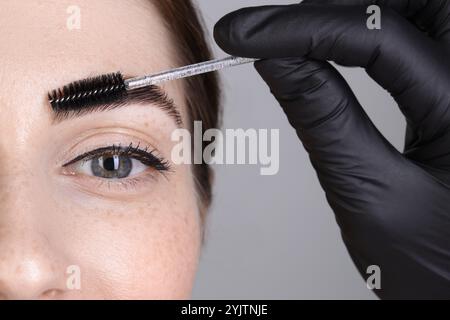 Brow lamination. Cosmetologist combing woman's eyebrows with brush ...