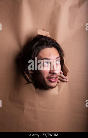 Man's head sticking out and looking through a paper hole with his hands ...