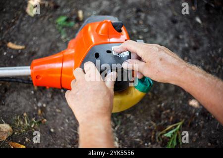 Starting a gas trimmer to mow the grass. A man opens the choke to make ...