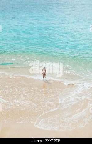 A blonde Caucasian woman exiting the ocean carrying a blue long surf ...