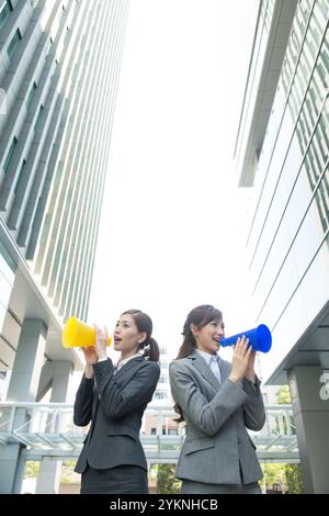 Two office workers shouting into a megaphone in an office building ...