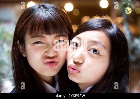 Two high school girls cheek to cheek, looking at each other and joking ...