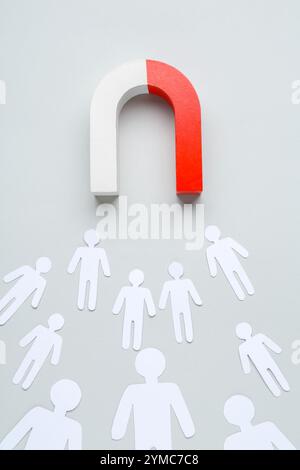 Magnet attracting paper cutouts of humans on light grey background ...