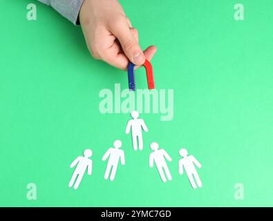 Man with magnet attracting paper human figures at green table, above ...