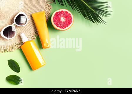 Orange sunblock package, sunglasses, straw hat and palm leaves on green ...
