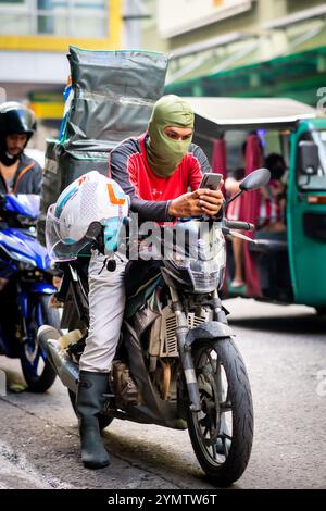 A Filipino bike courier takes a break to check his phone on the busy ...