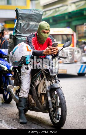 A Filipino bike courier takes a break to check his phone on the busy ...
